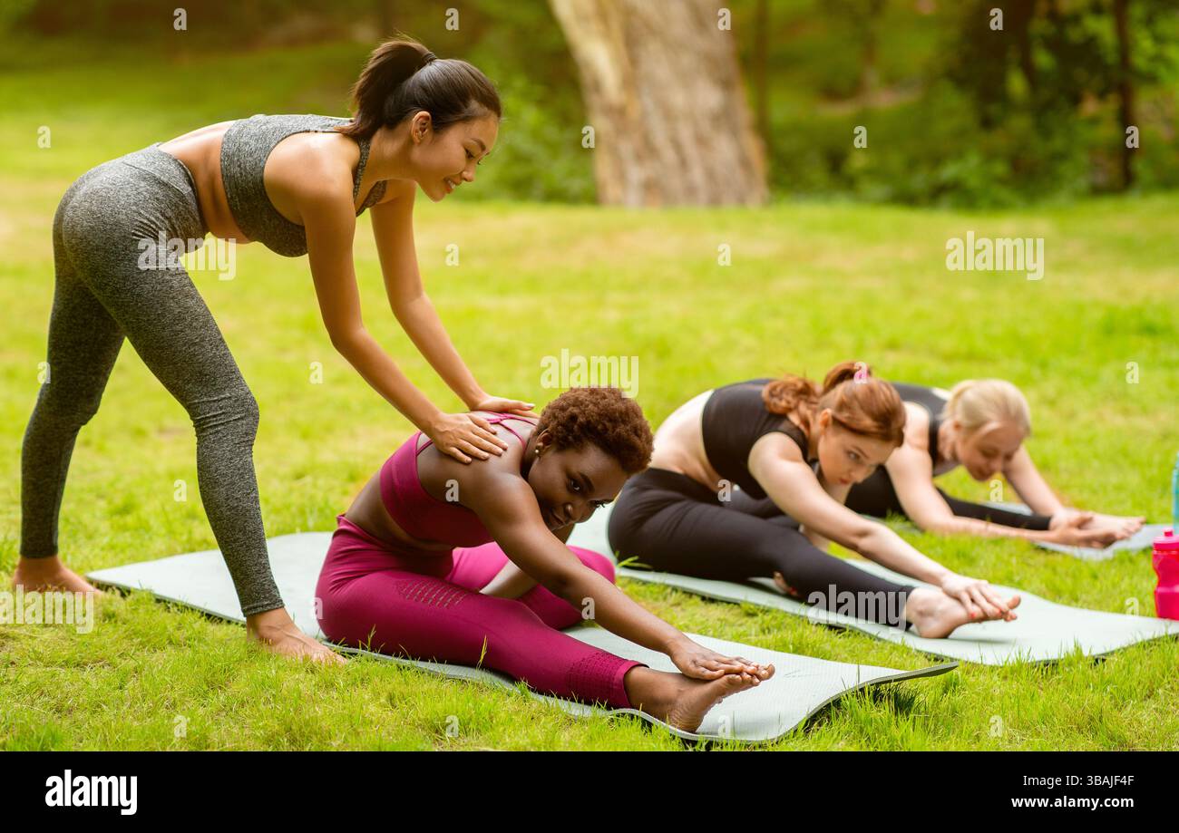 Young female yoga instructor teaching group of sporty women to do ...