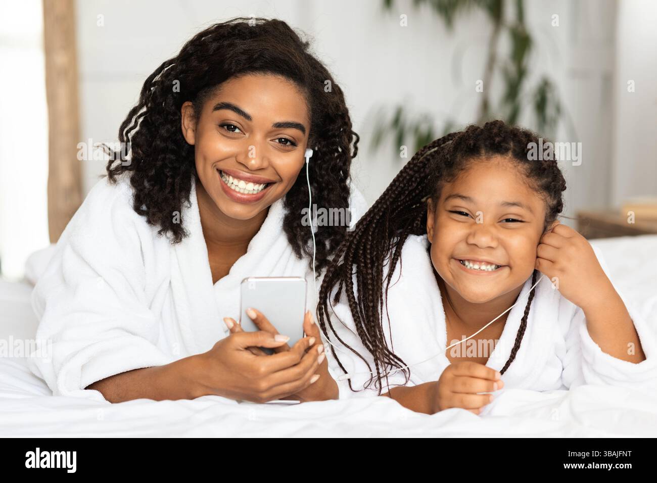 Joyful African Mother And Little Daughter Relaxing With Smartphone, Listening Music, Sharing ...