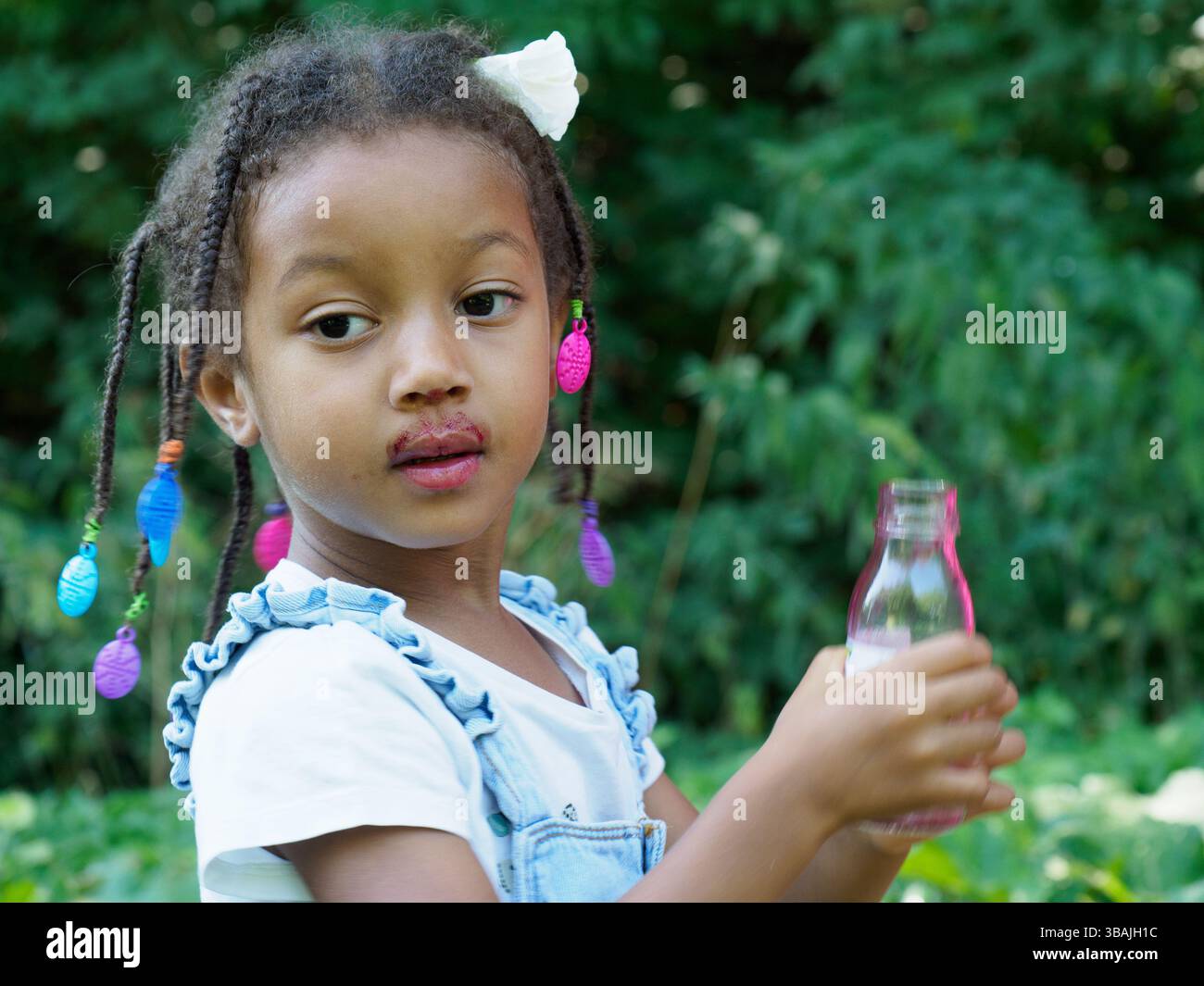 Side view of Black little girl with braids holding juice bottle ...