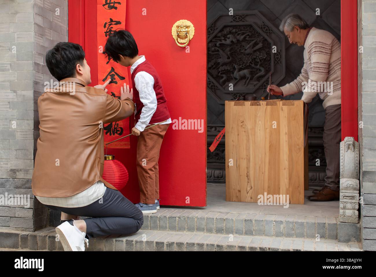 Chinese father and son decorating door while grandfather is writing ...