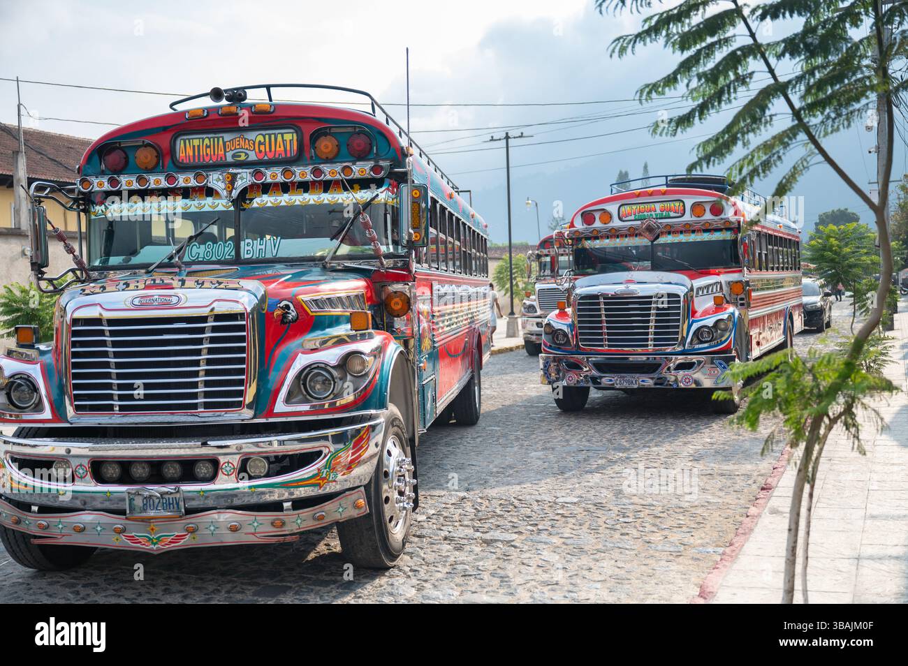Brightly decorated chicken buses parked in a cobblestone street of ...
