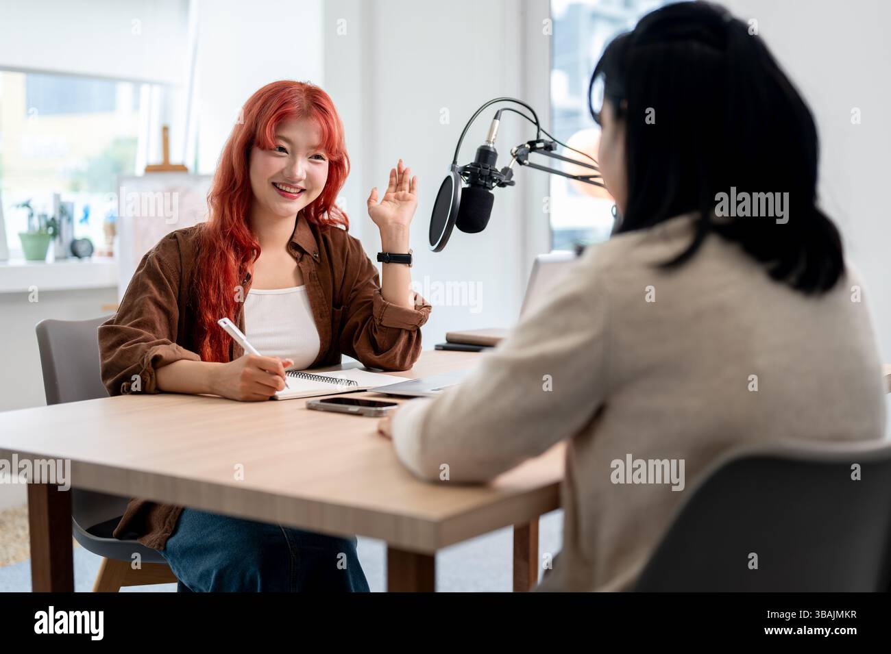 A beautiful Asian female podcaster with red curly hair is interviewing ...
