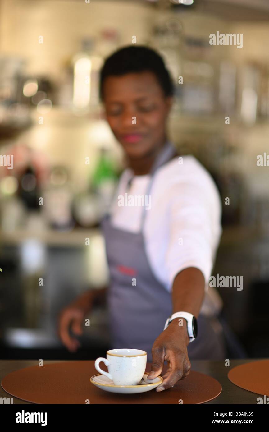 Black female barista with short hair wearing apron serving cup of ...