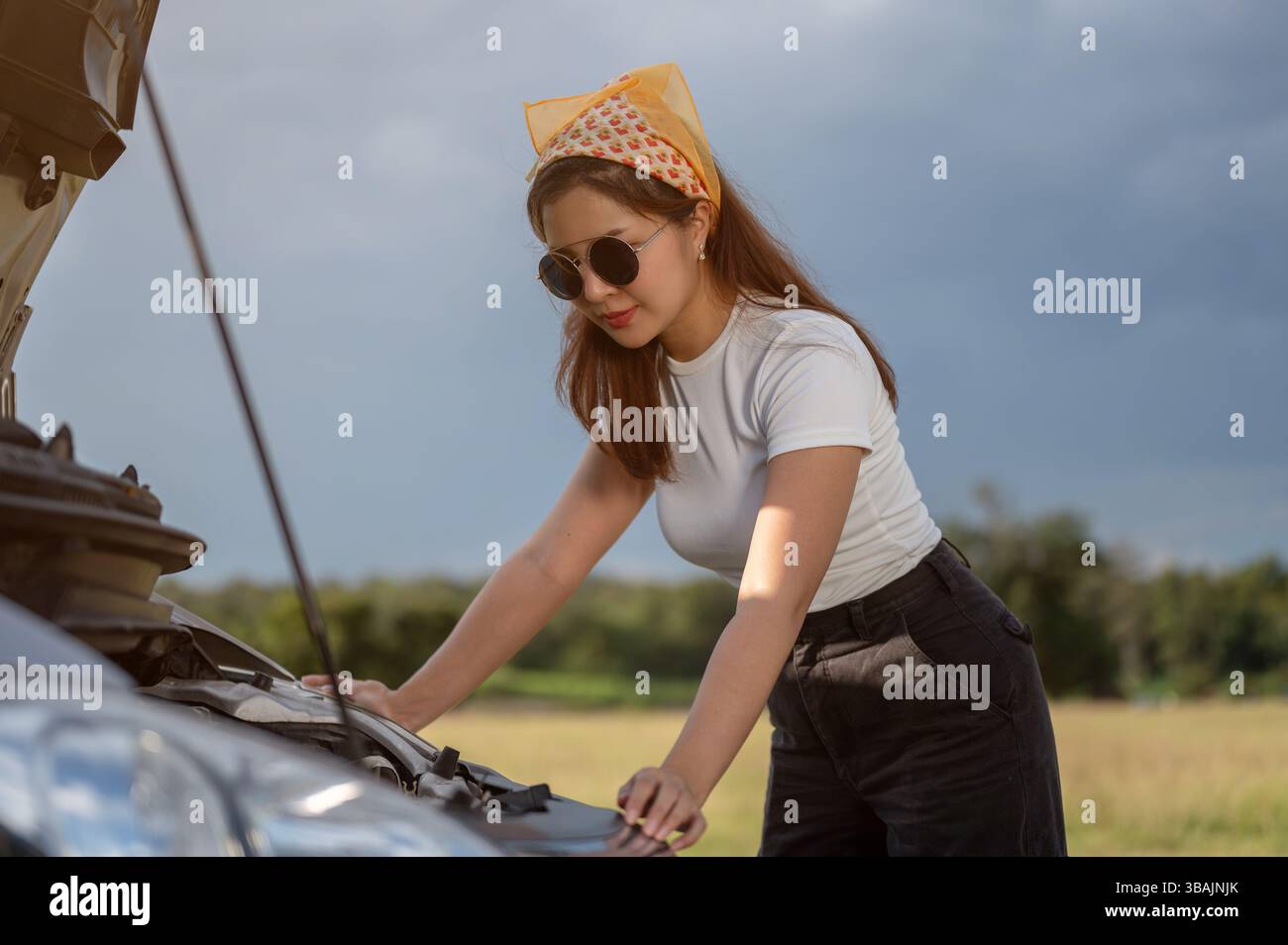 An attractive young Asian woman is checking her car engine after a long travel to the ...