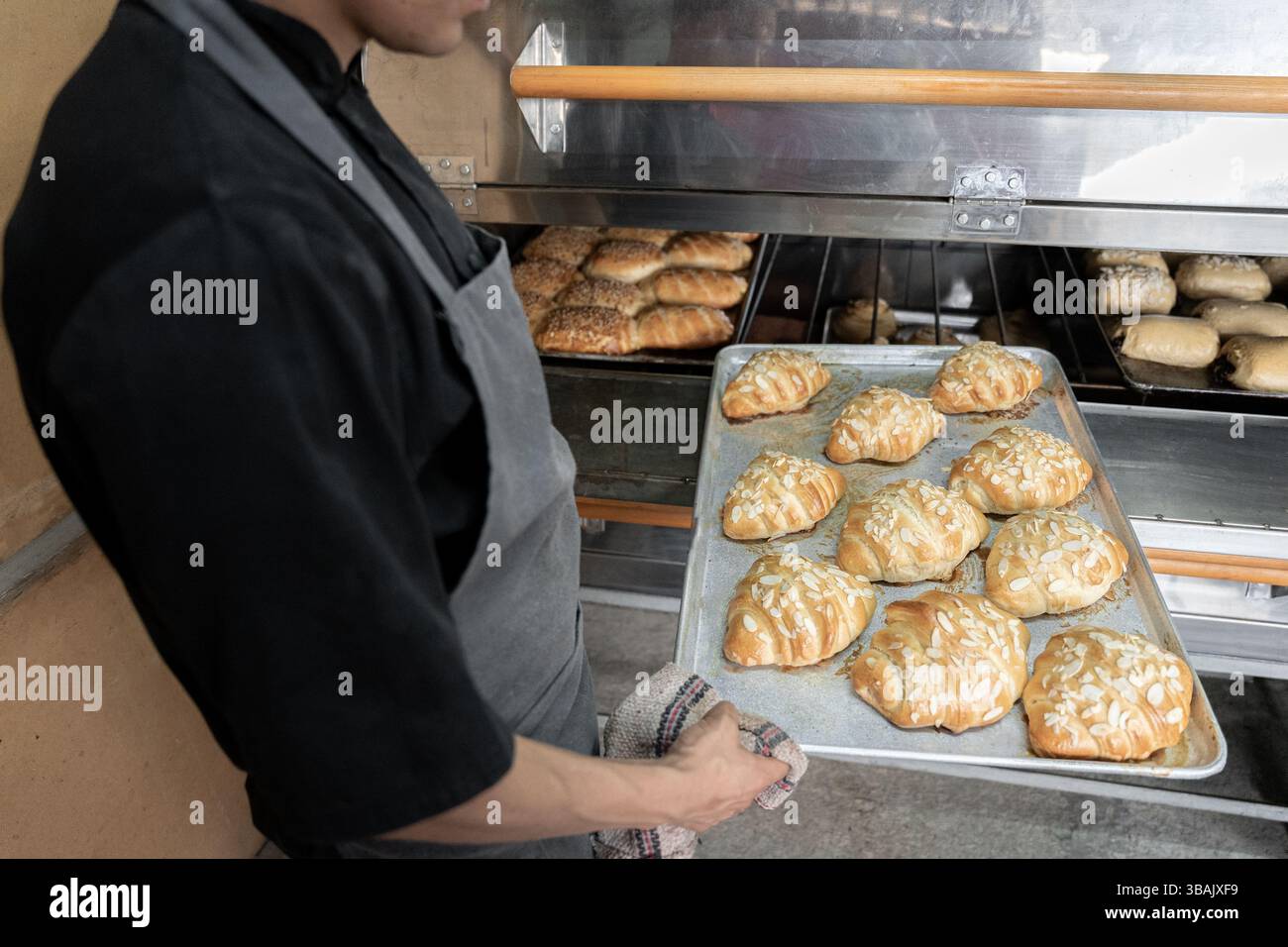 Hispanic baker is opening the oven door to check the croissants baking ...