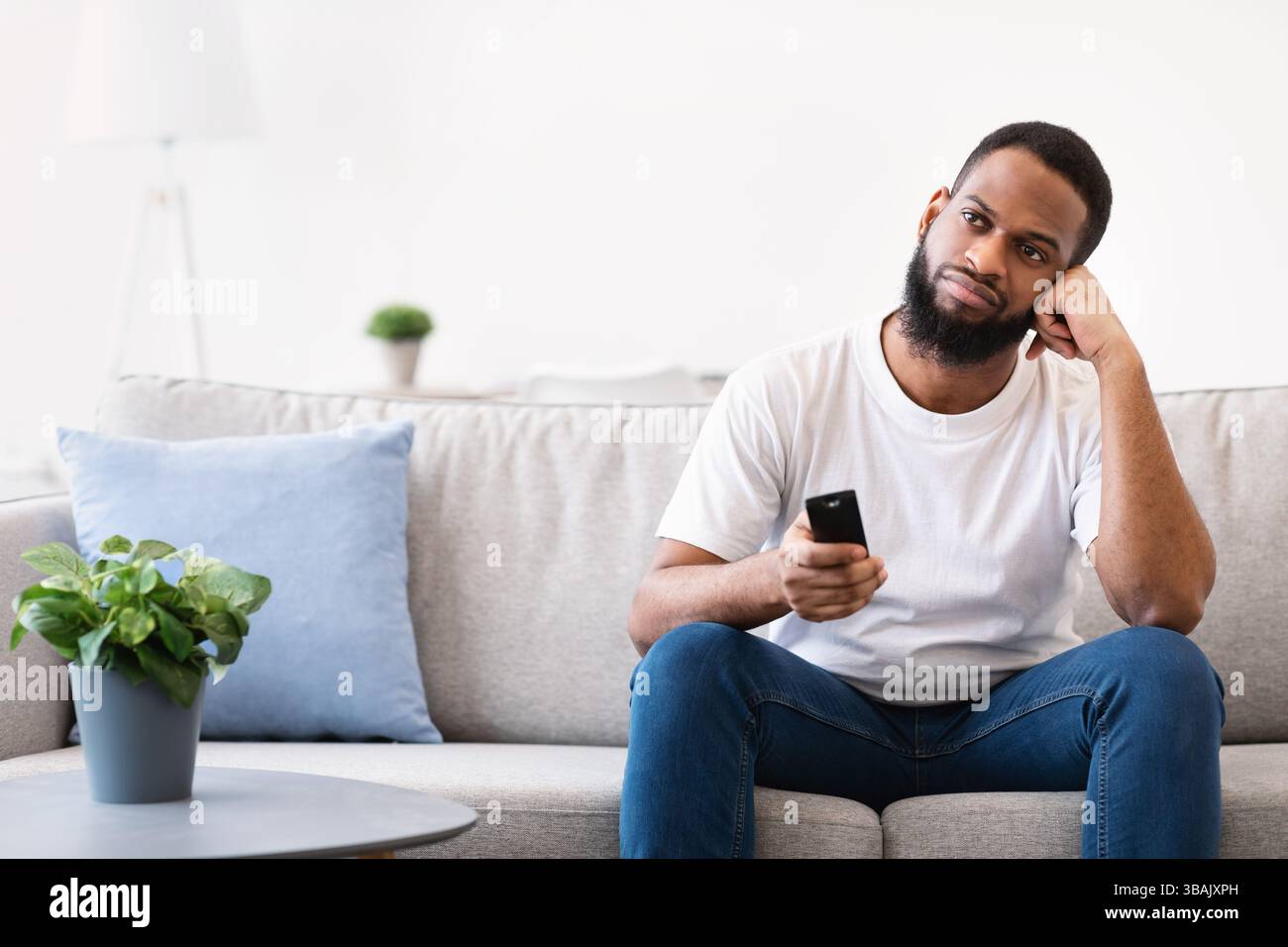 Bored African Man Watching TV Switching Television Channels With Remote Control Sitting On Couch ...