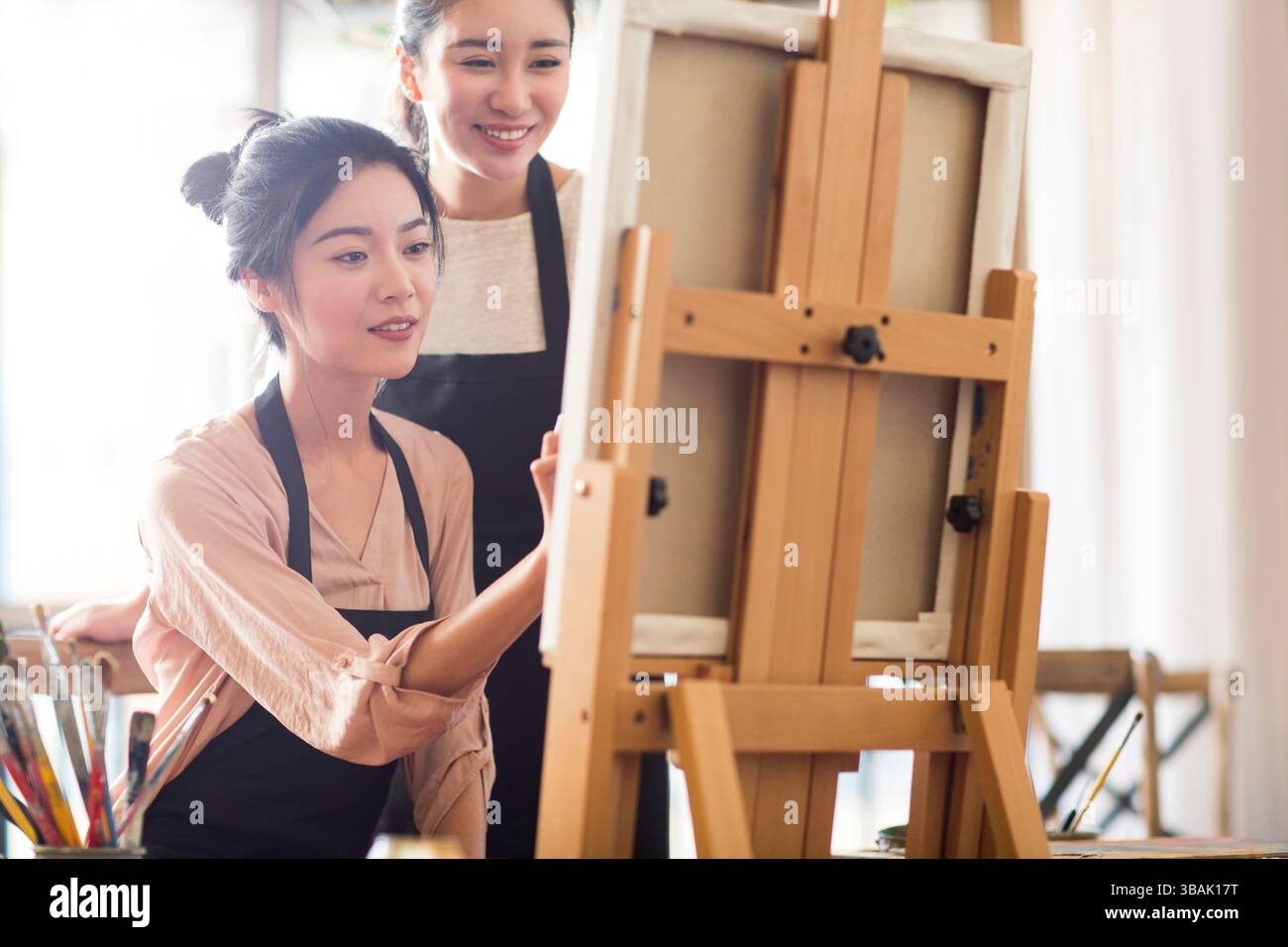 Chinese woman painting on canvas with female classmate watching her ...