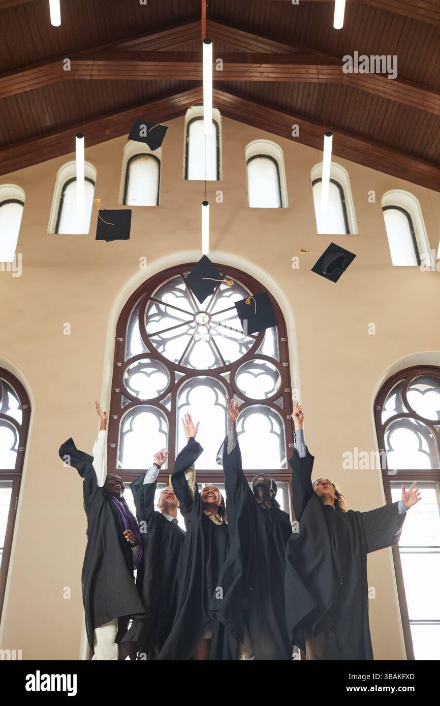Diverse group of students wearing graduation gowns throwing their caps ...
