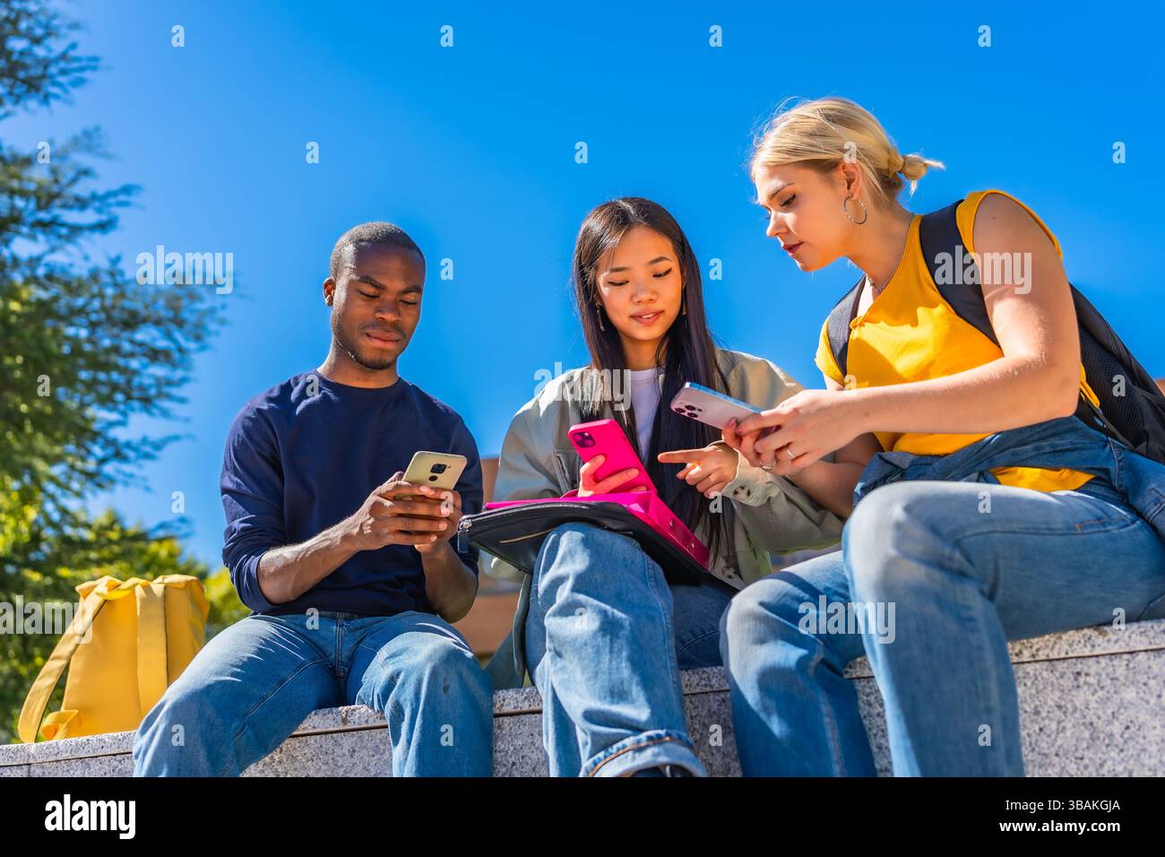 Low angle view photo of a group of students using mobile phone sitting ...