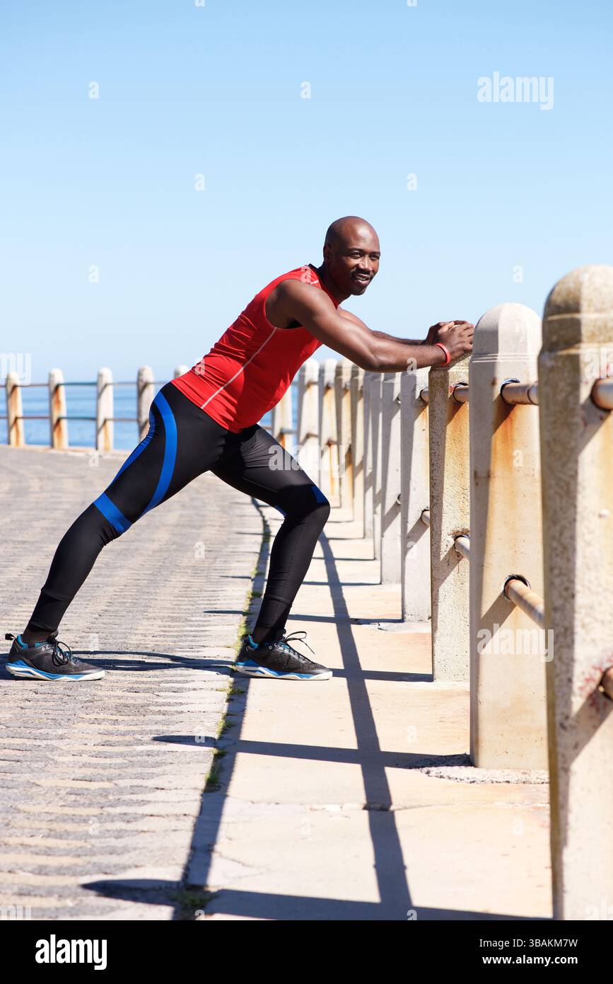 Full length portrait of fit african man doing stretching on railing at ...