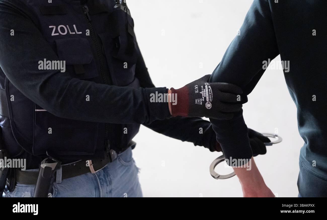 Munich, Germany. 12th May, 2025. A customs investigator handcuffs a man ...