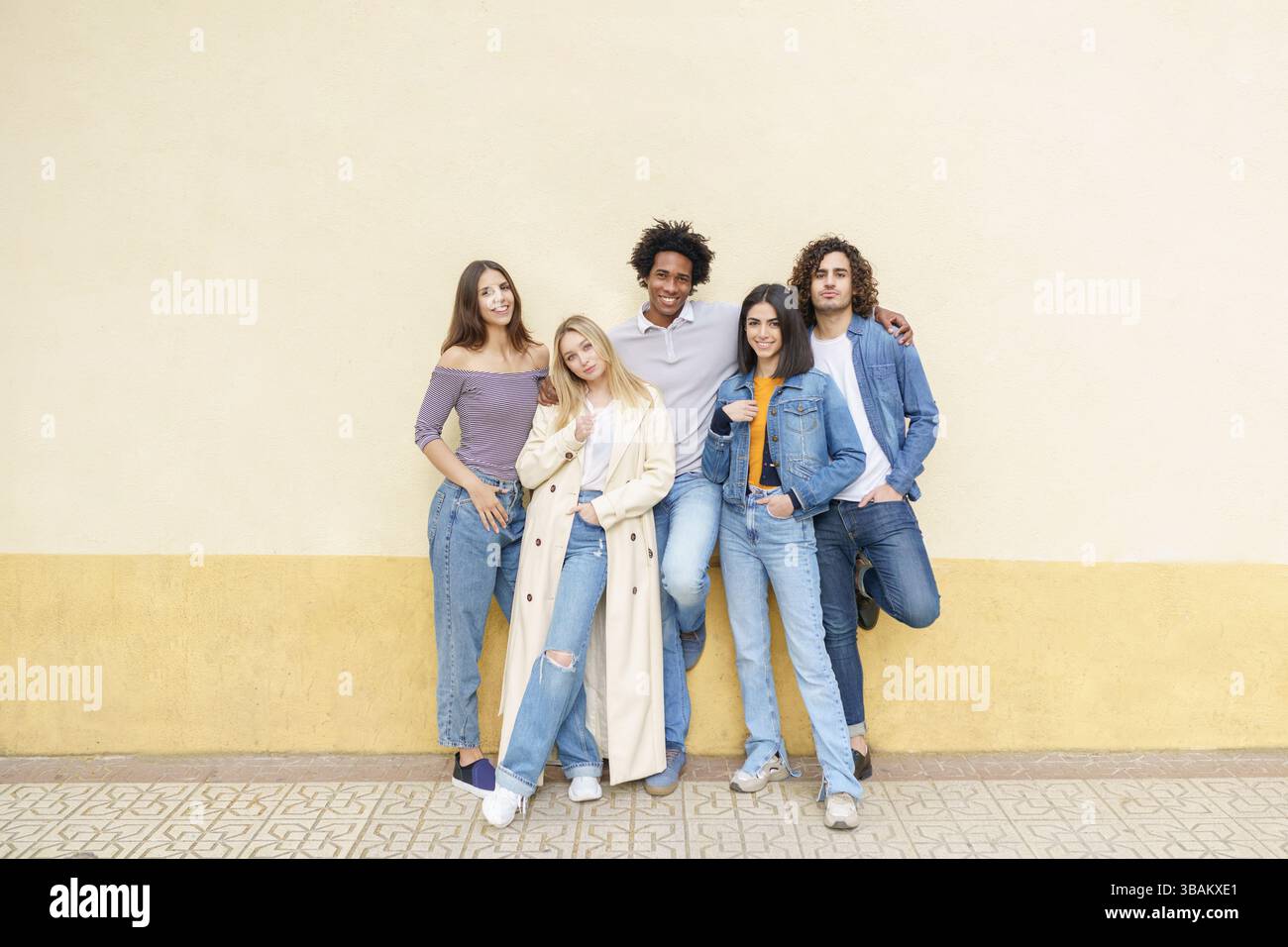 Group of diverse friends standing close together against wall outdoors ...