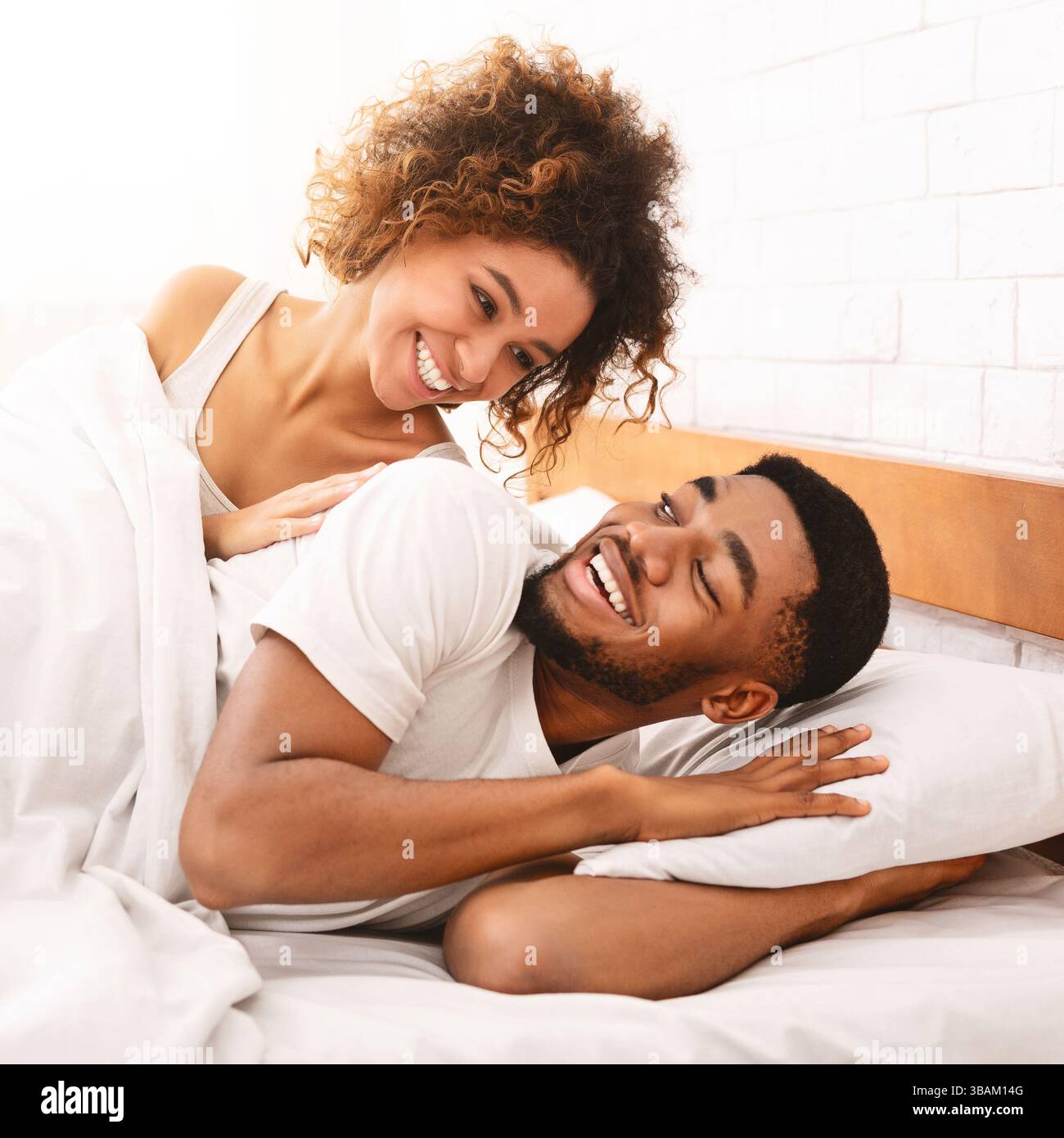Happy morning. Laughing african-american couple waking up in bed ...