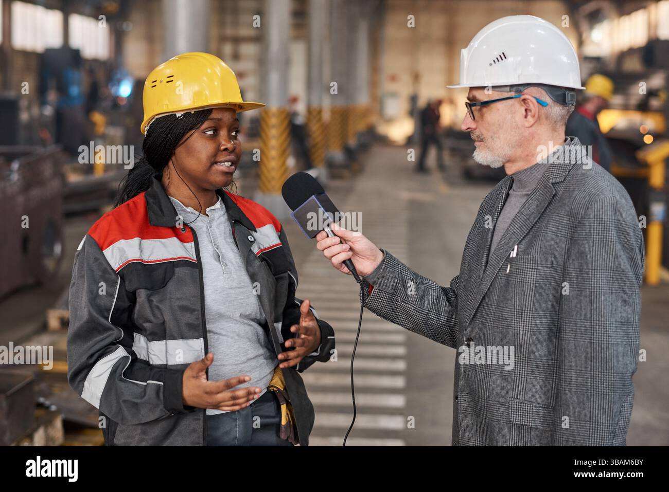 News reporter in work helmet holding microphone in front of the worker ...