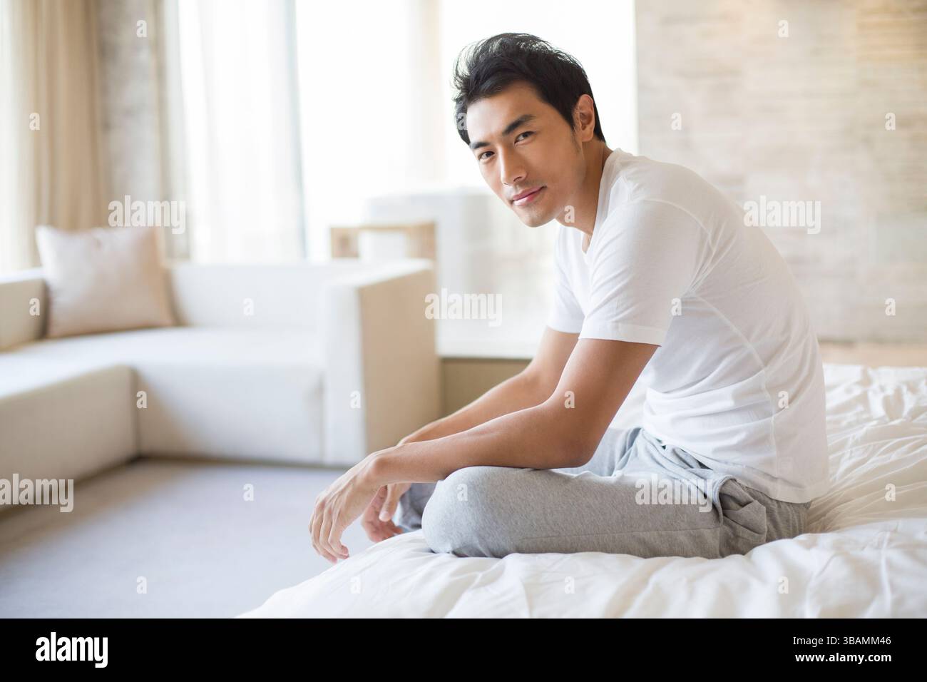 Young Chinese man sitting on bed Stock Photo - Alamy