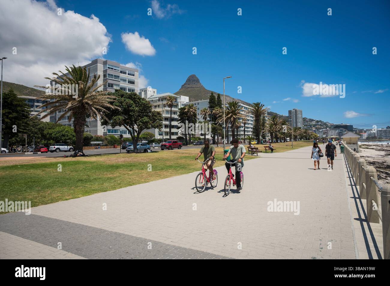 People cycle and ride bikes along the beach sea wall in the Sea Point ...
