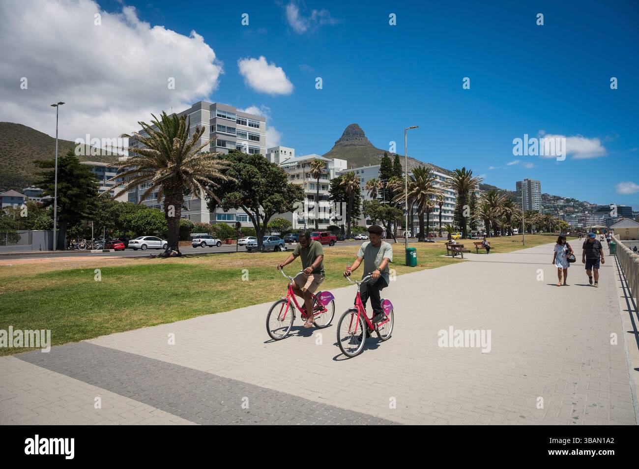 People cycle and ride bikes along the beach sea wall in the Sea Point ...