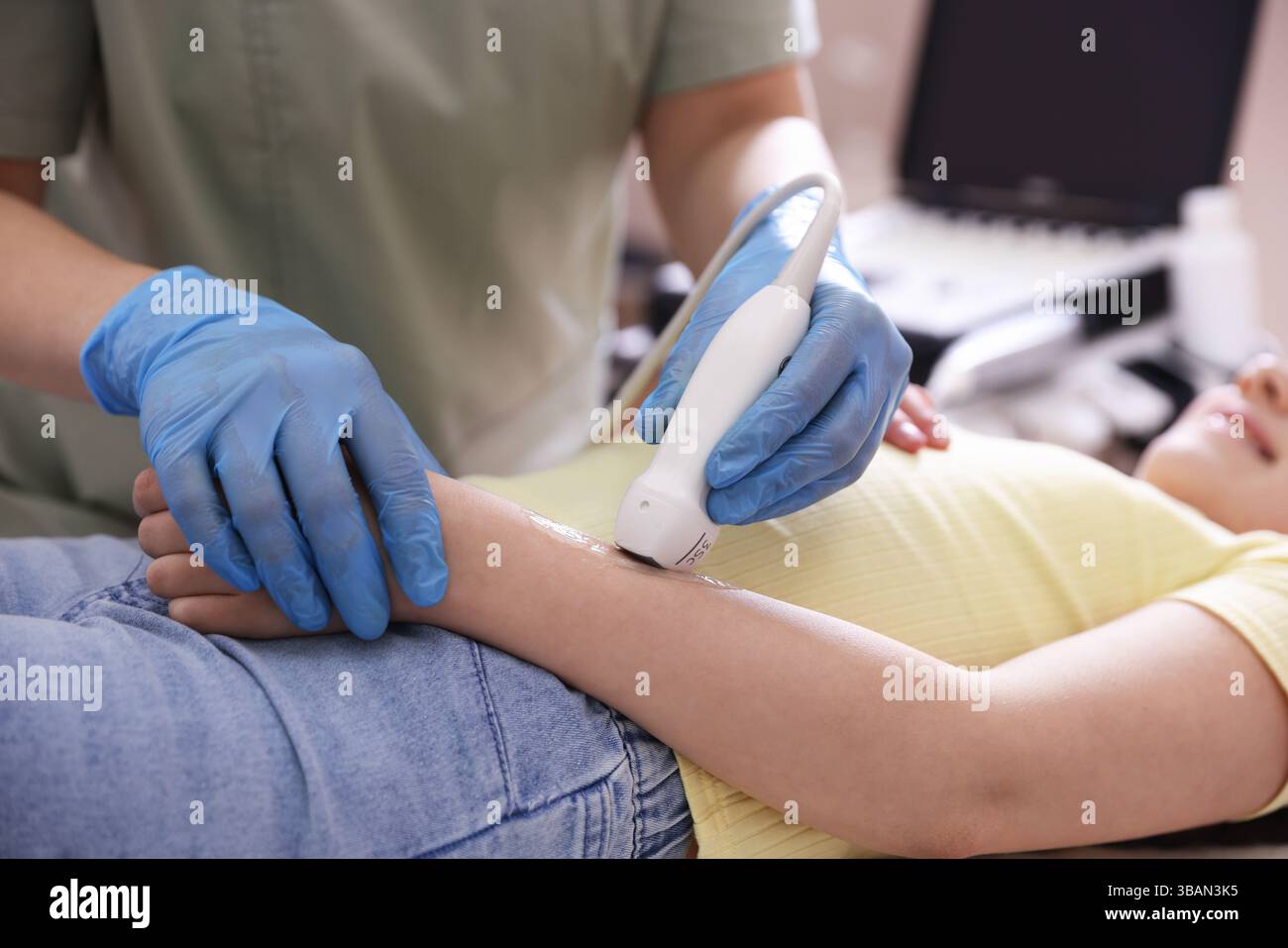 Sonographer conducting ultrasound examination of girl's arm in clinic ...