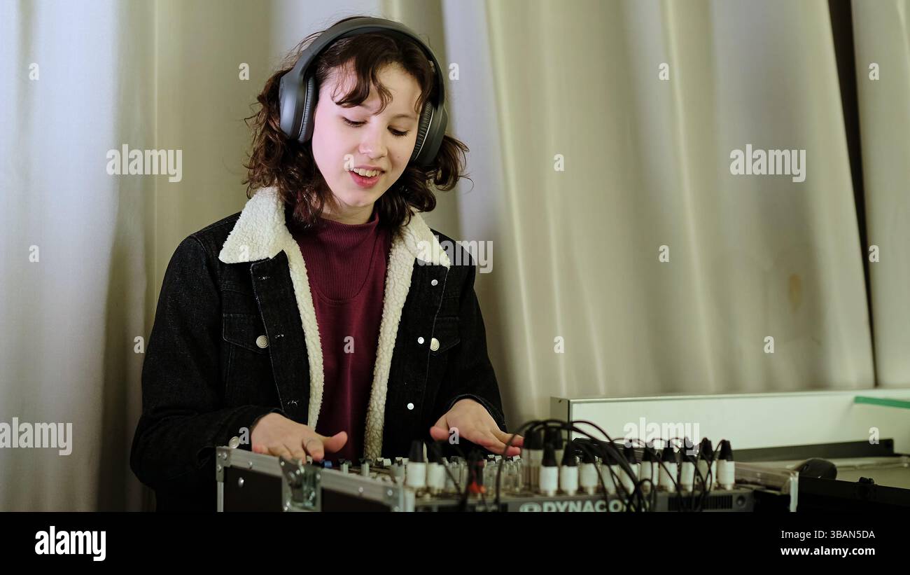 A girl leans over a soundboard, her hands on the controls and a smile ...