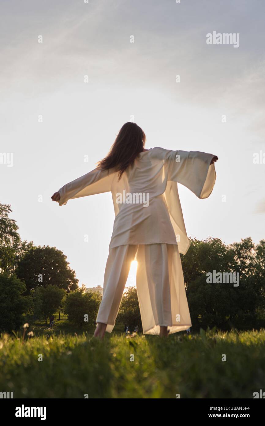 A person in flowing white garments extends their arms in a wide gesture ...
