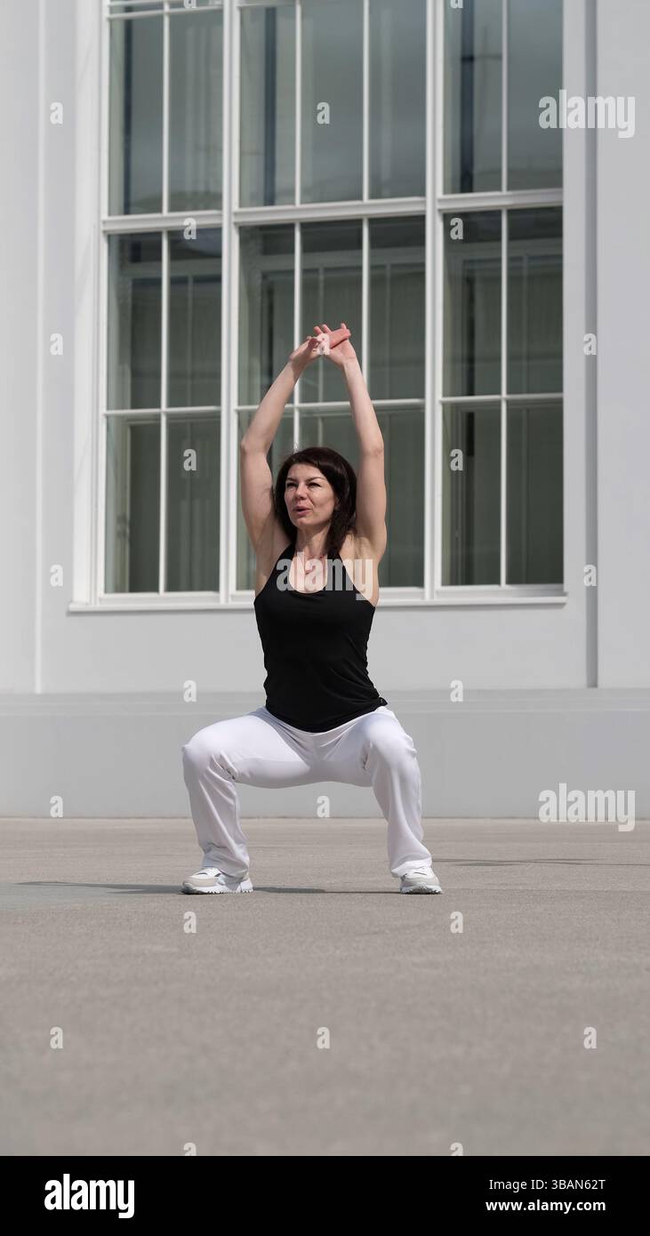 A woman performs a deep squat with her arms extended overhead, engaging ...