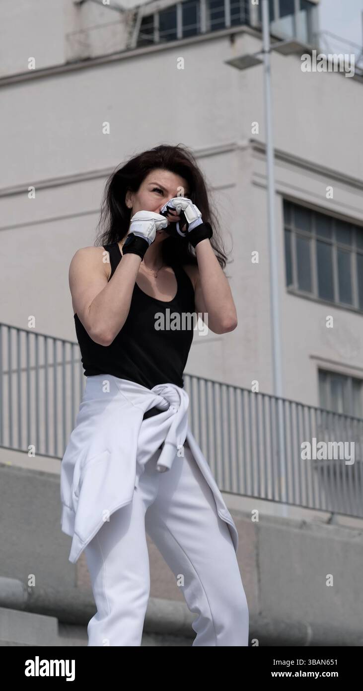 A woman with an athletic build playfully strikes a boxing pose outdoors ...
