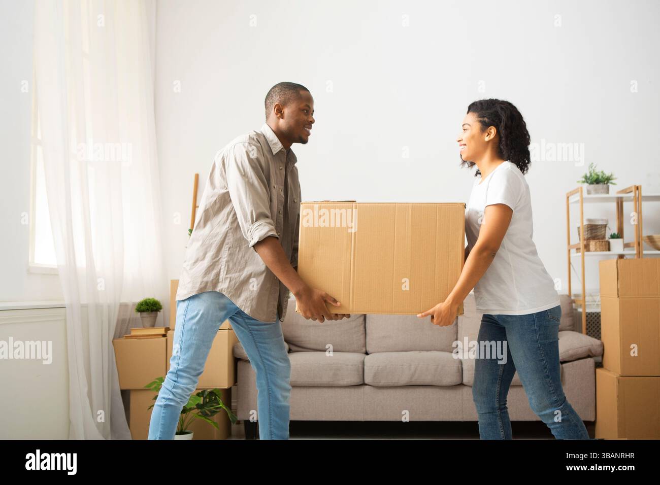 Black couple walking and carrying big box together moving into their ...