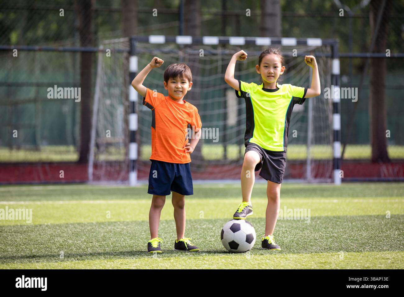 Chinese children with football flexing biceps standing on field during ...