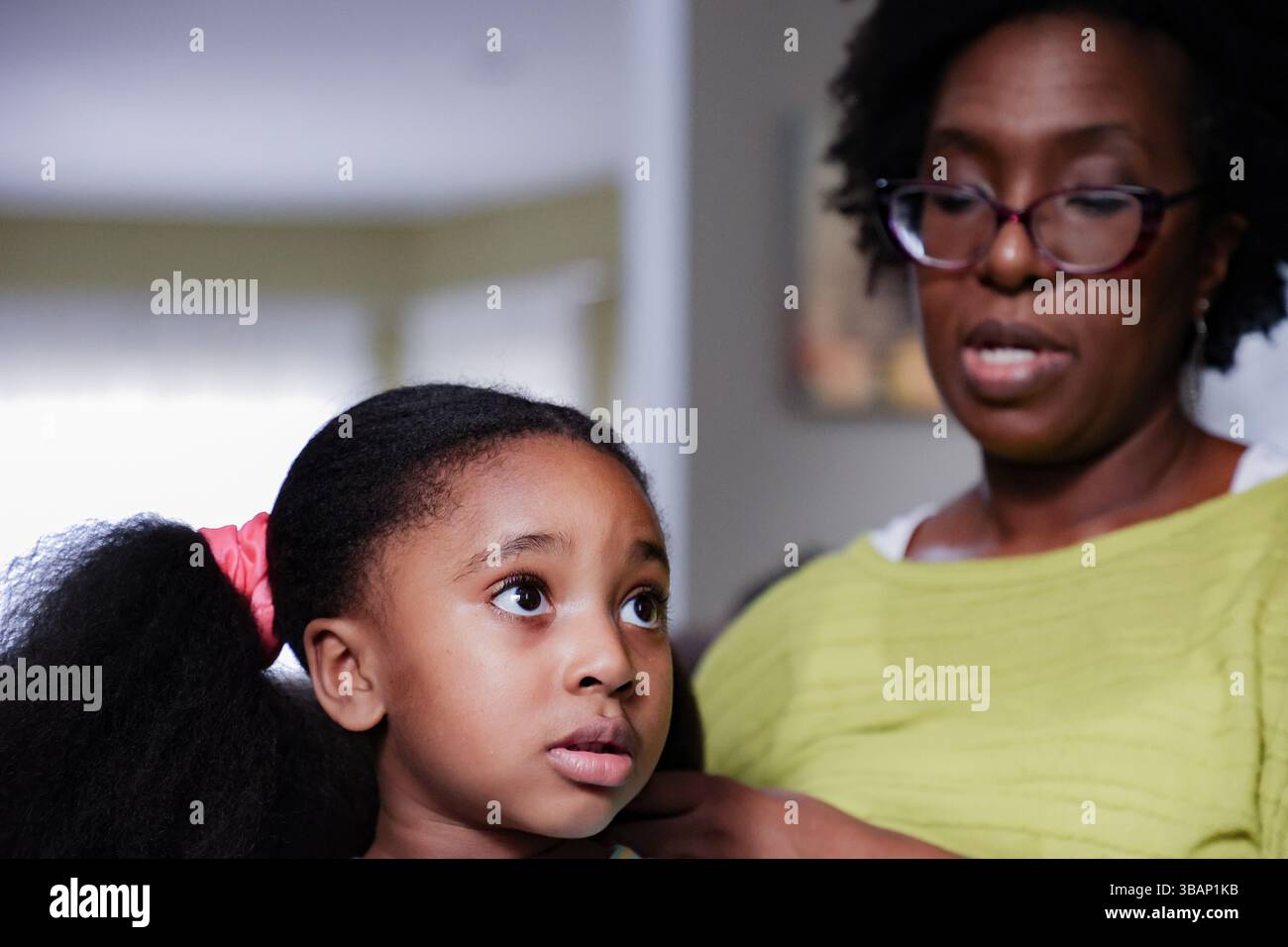 Black daughter with hair being fixed by mother while sitting together on sofa at home Stock ...