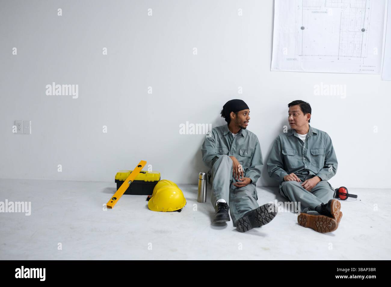 Black and Asian male construction workers chatting while sitting on ...