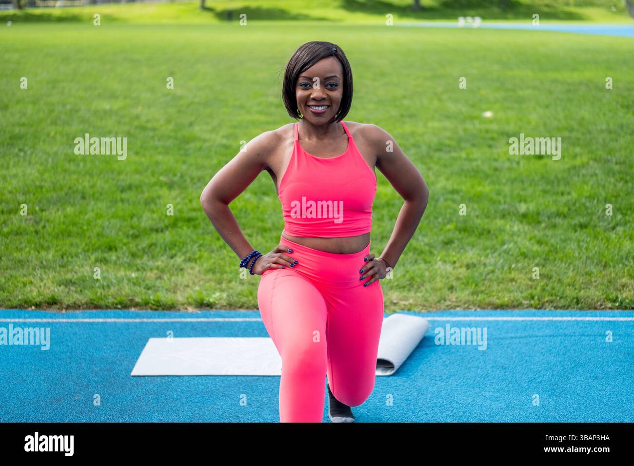 Smiling Black woman in pink activewear bending her legs with hands on ...