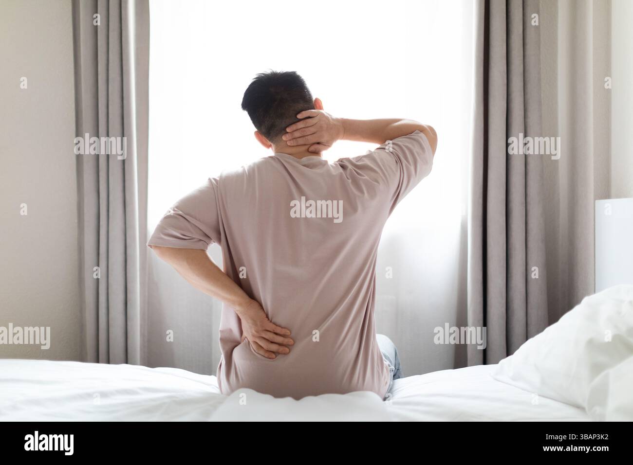 Tired man suffering from back pain after sleeping in bedroom, waking up ...
