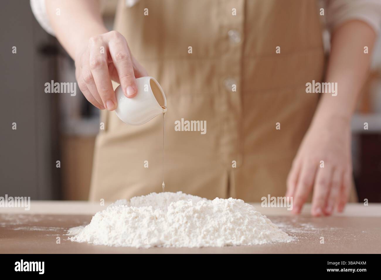 Woman pouring vegetable oil in well she made in pile of flour when ...