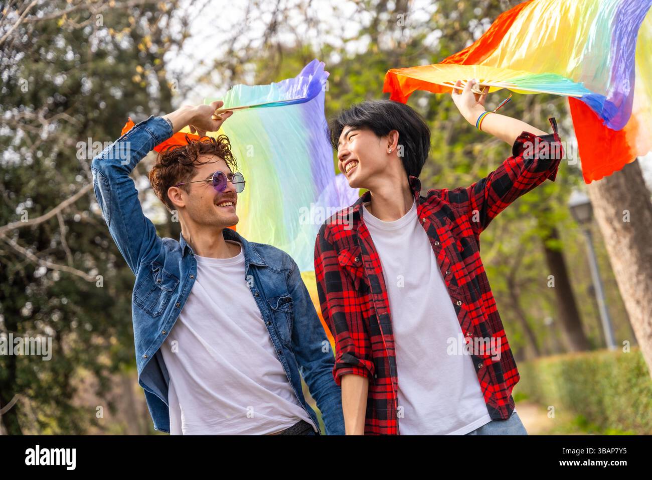 Gay couple holding hands strolling happily in a park raising lgbt ...