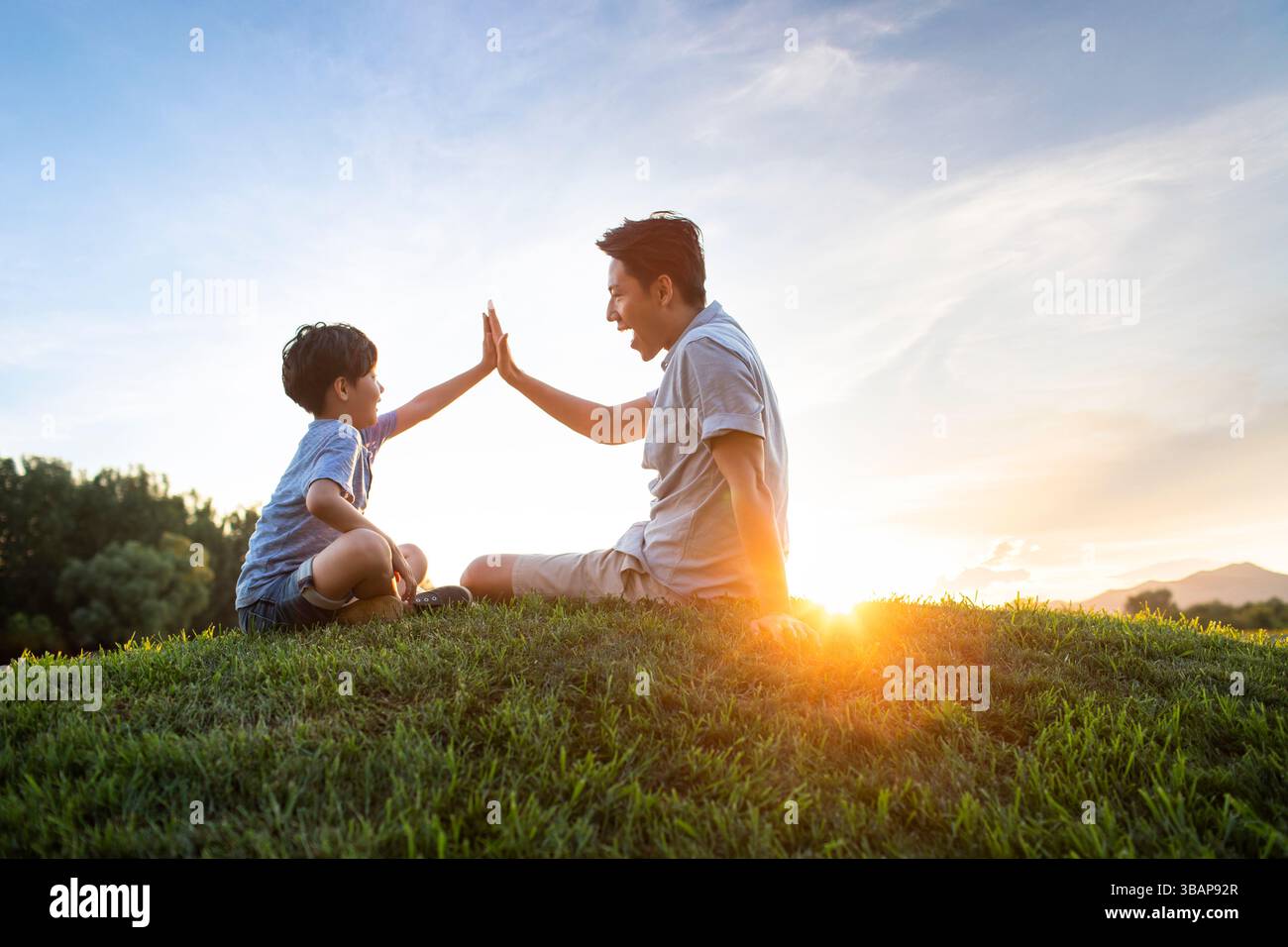 Smiling Chinese father giving high five to his son while sitting on the ...