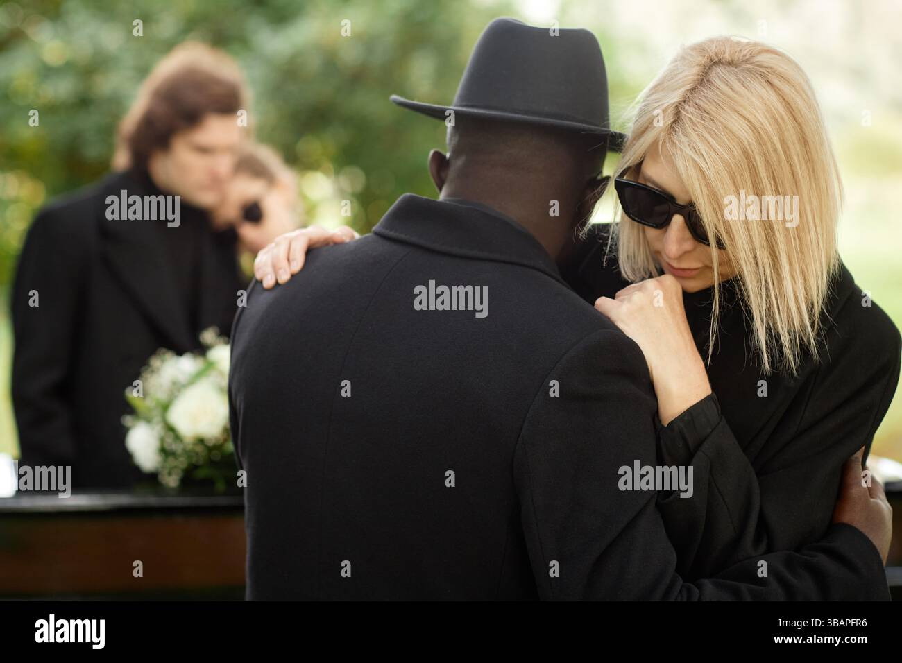 Two people embracing at outdoor funeral ceremony and wearing black ...