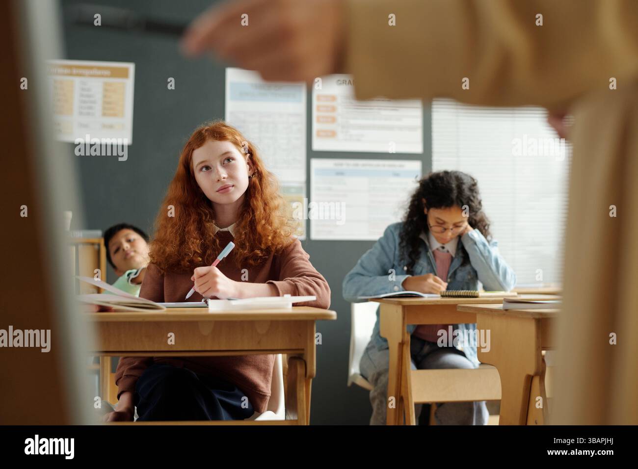 Clever schoolgirl with pen listening to explanation of teacher and ...