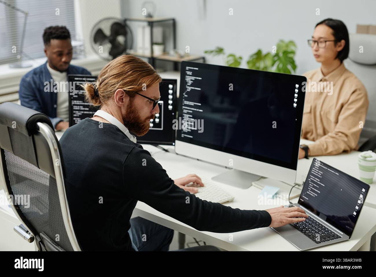Young serious diversity programmer typing on laptop keyboard while sitting in front of computers ...