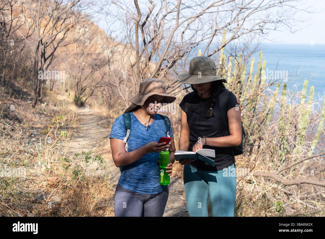 Two female hikers with hats using a smartphone and a paper map to ...