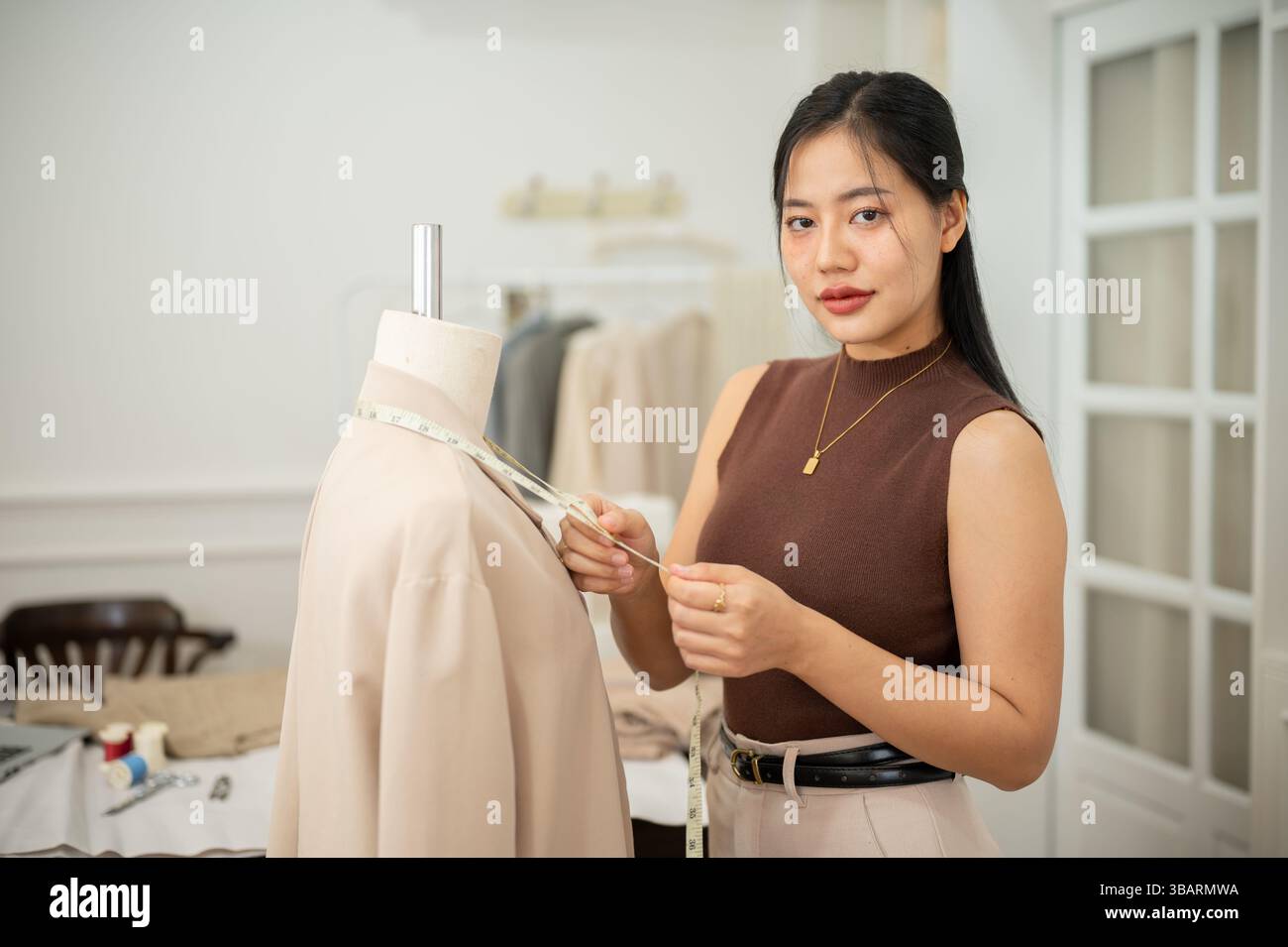 A professional and confident Asian female tailor or fashion designer is working in her studio ...