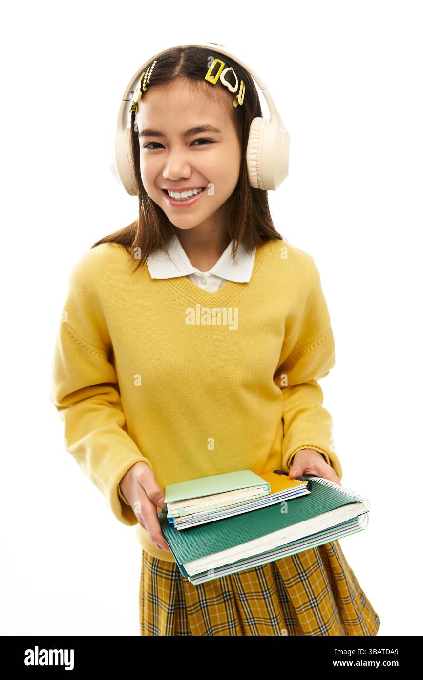 A cheerful asian schoolgirl in a yellow sweater and plaid skirt wears ...