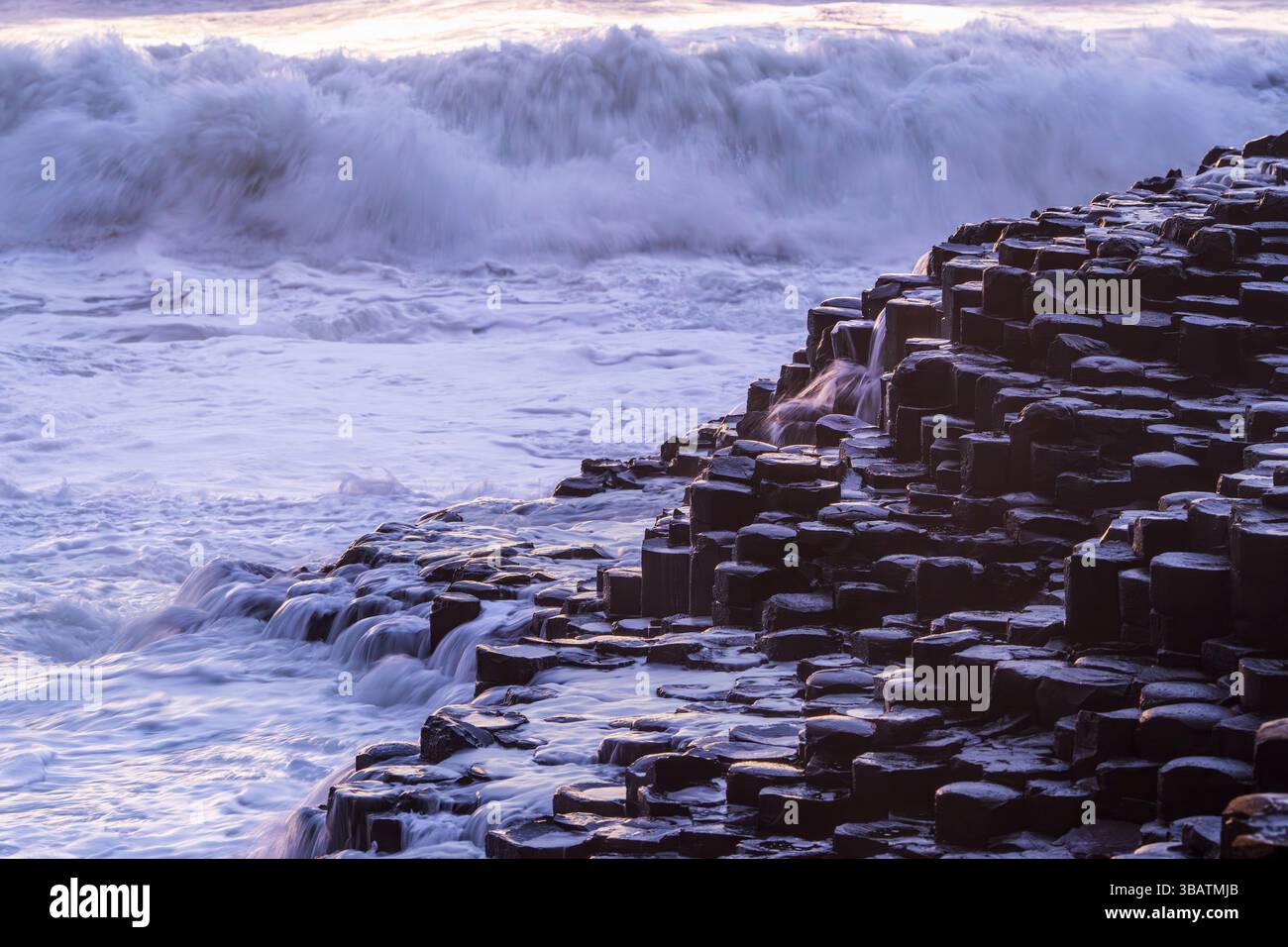 Close up of interlocking basalt columns of Grand Causeway at dusk, as waves break. Giant's ...