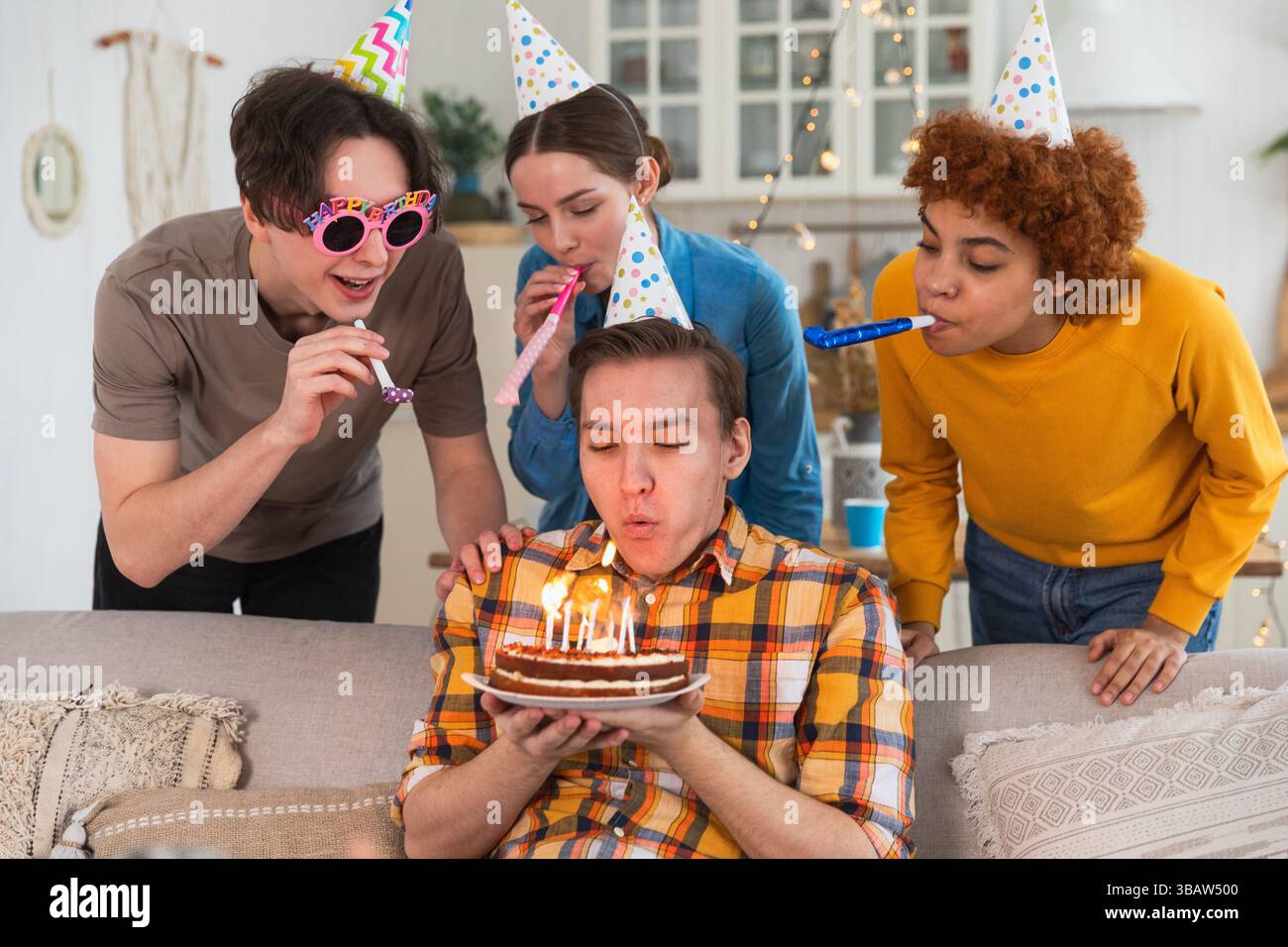 Make a wish. Man wearing party cap blowing out burning candles on birthday cake. Happy Birthday ...