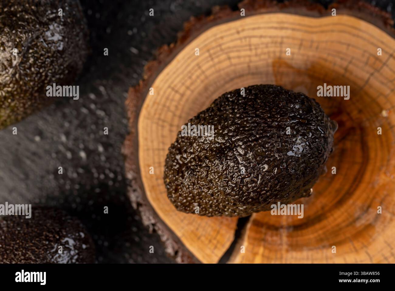 wet black avocado fruits of small size on a black slate, ripe avocado ...
