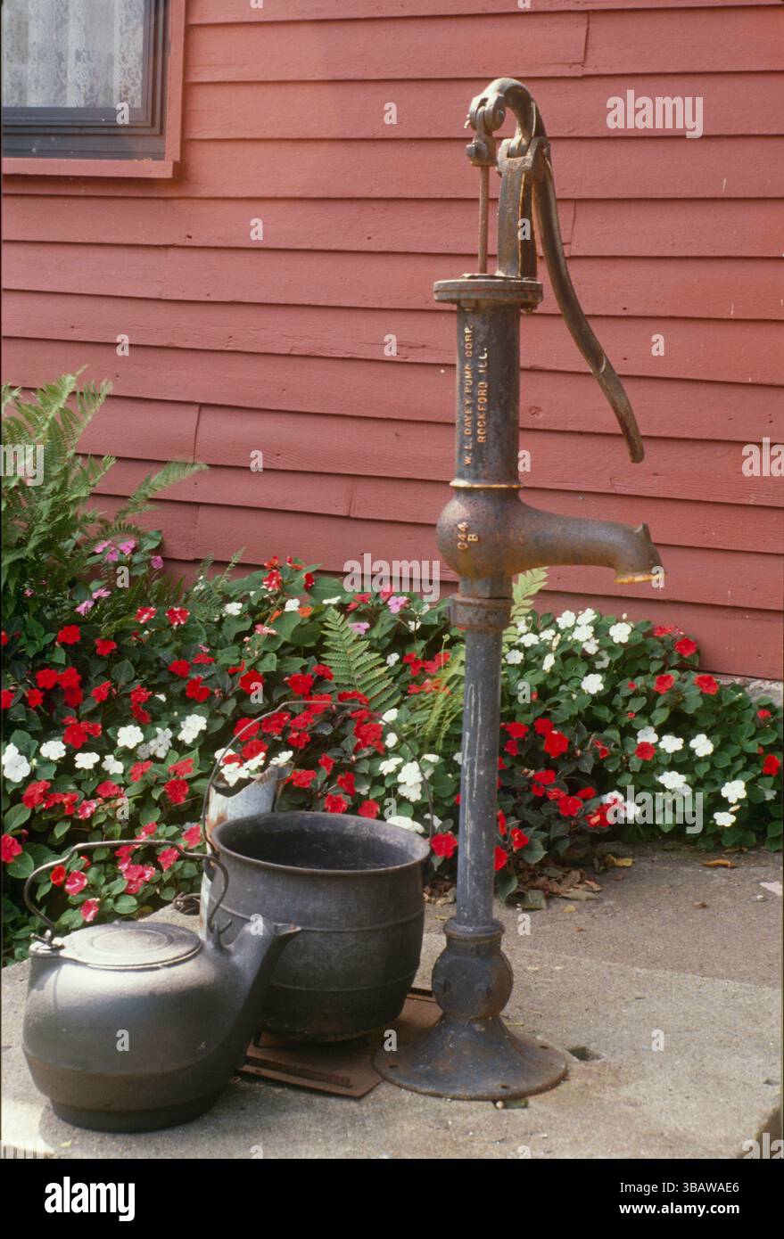 An old hand pump and metal pot to collect drinking water outside of a ...