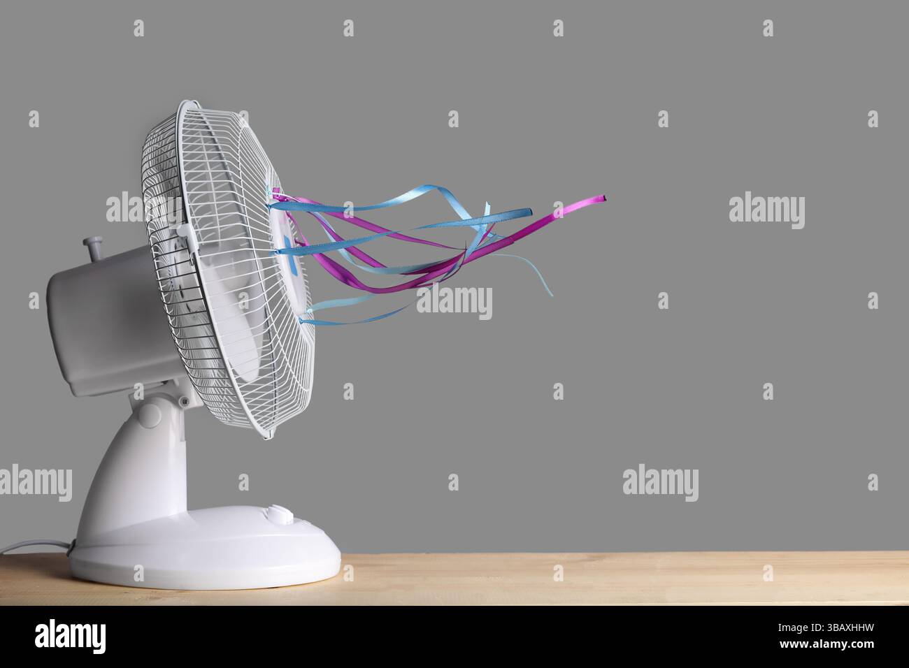 Electric fan with fluttering ribbons on table against grey background ...