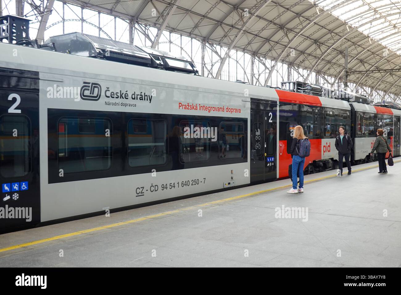 Passengers with luggage walk and wait on a covered platform between ...