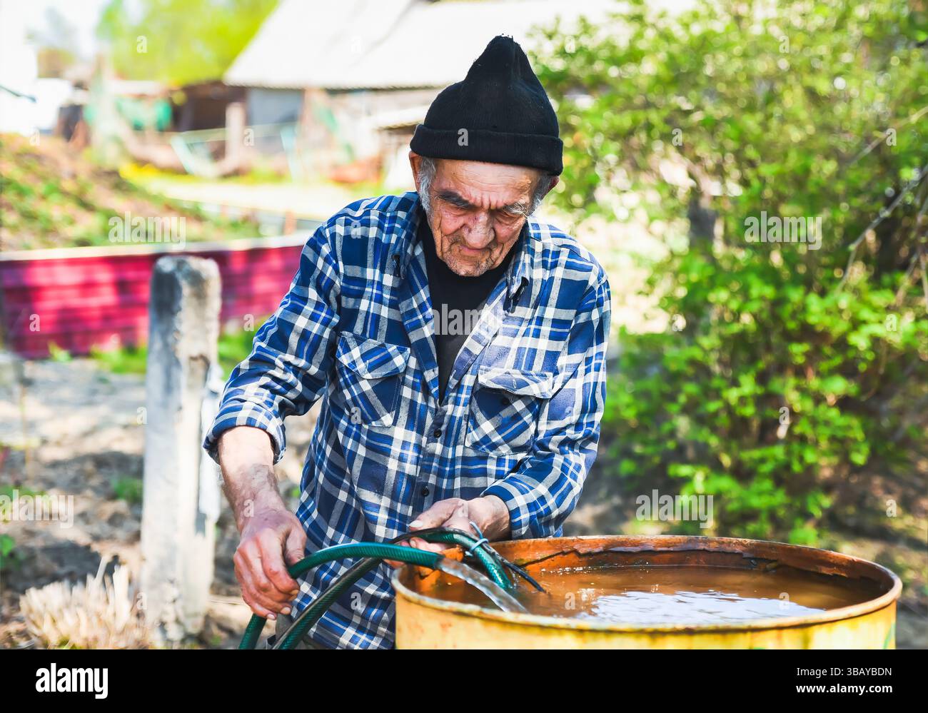 Elderly Russian man in a plaid shirt working with a drainage pump near ...