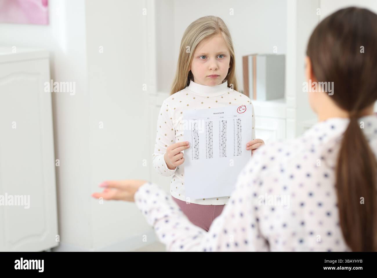 School grade. Sad girl showing answer sheet with bad mark to her mother ...