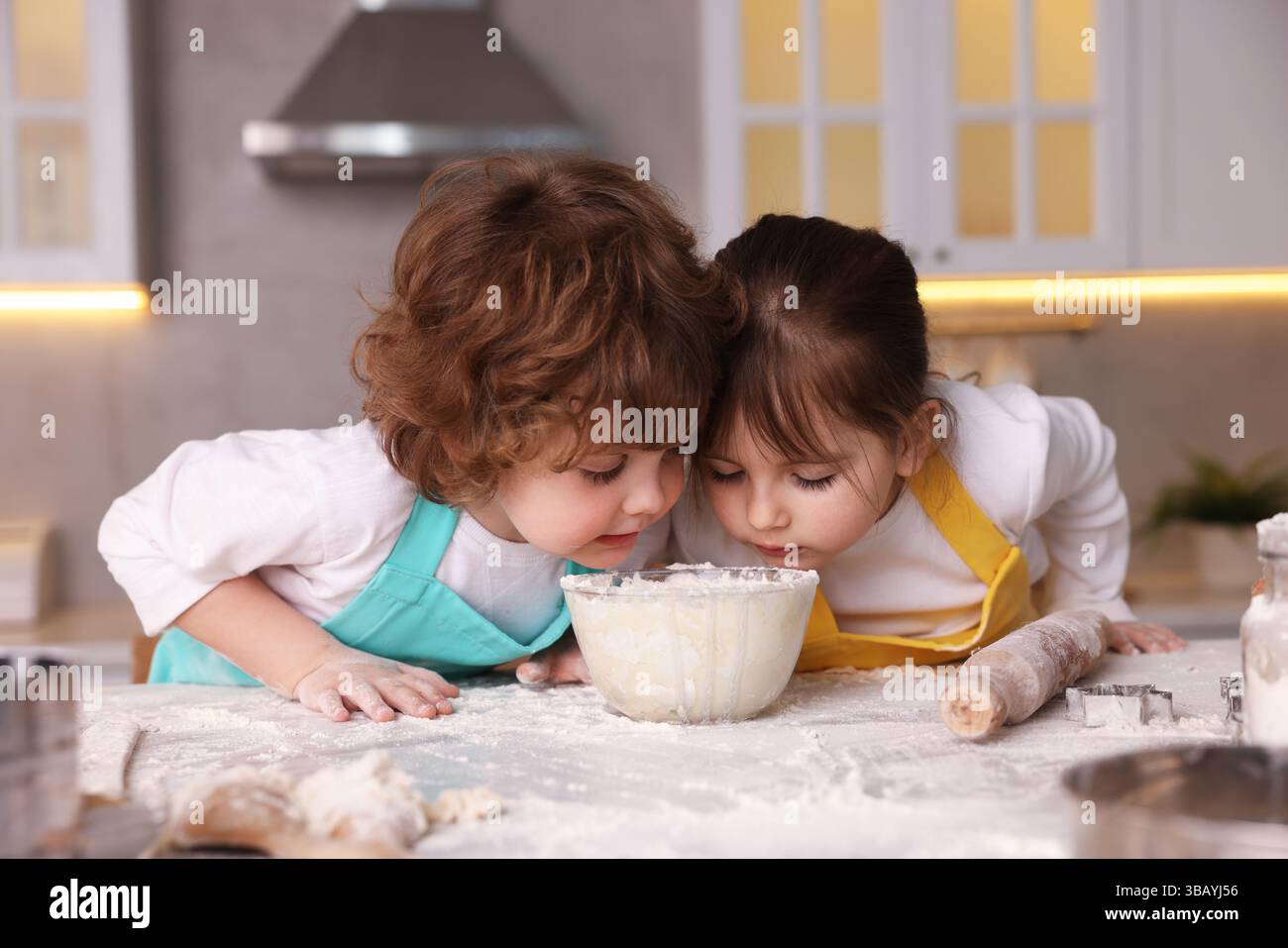 Cooking recipe. Little children smelling dough at table in kitchen ...